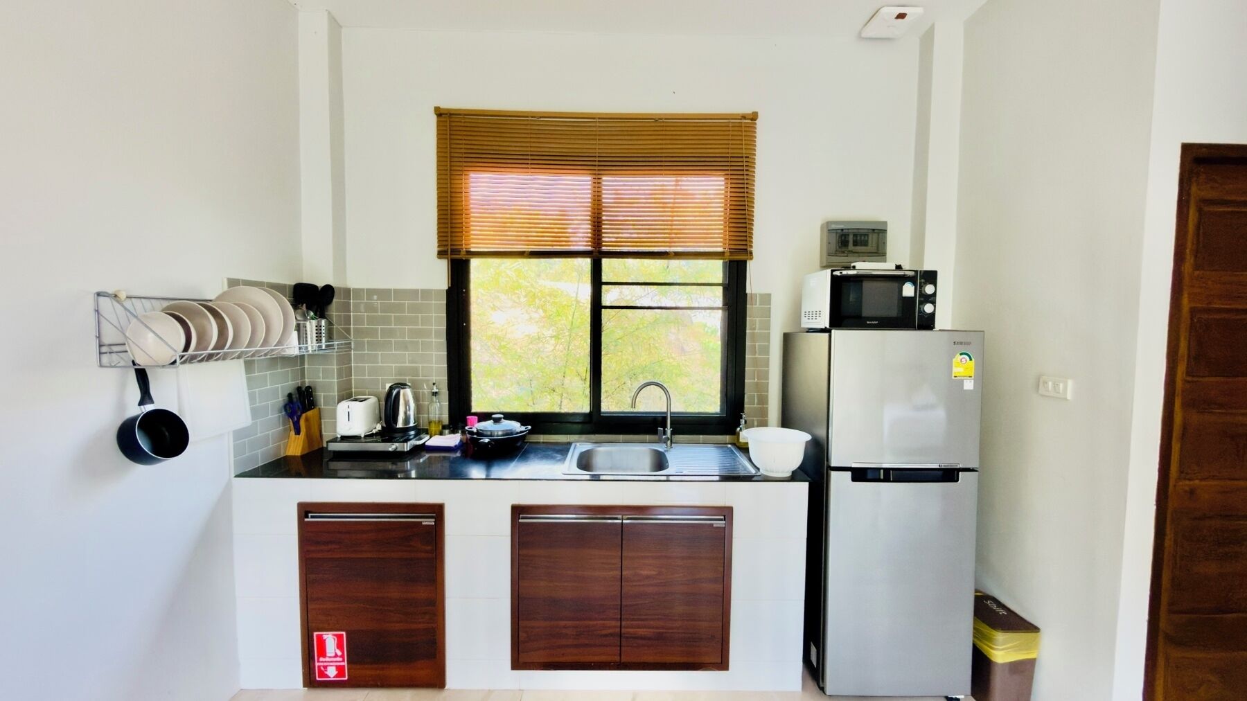 Uma cozinha compacta com pia, fogão, micro-ondas e janela com persianas.