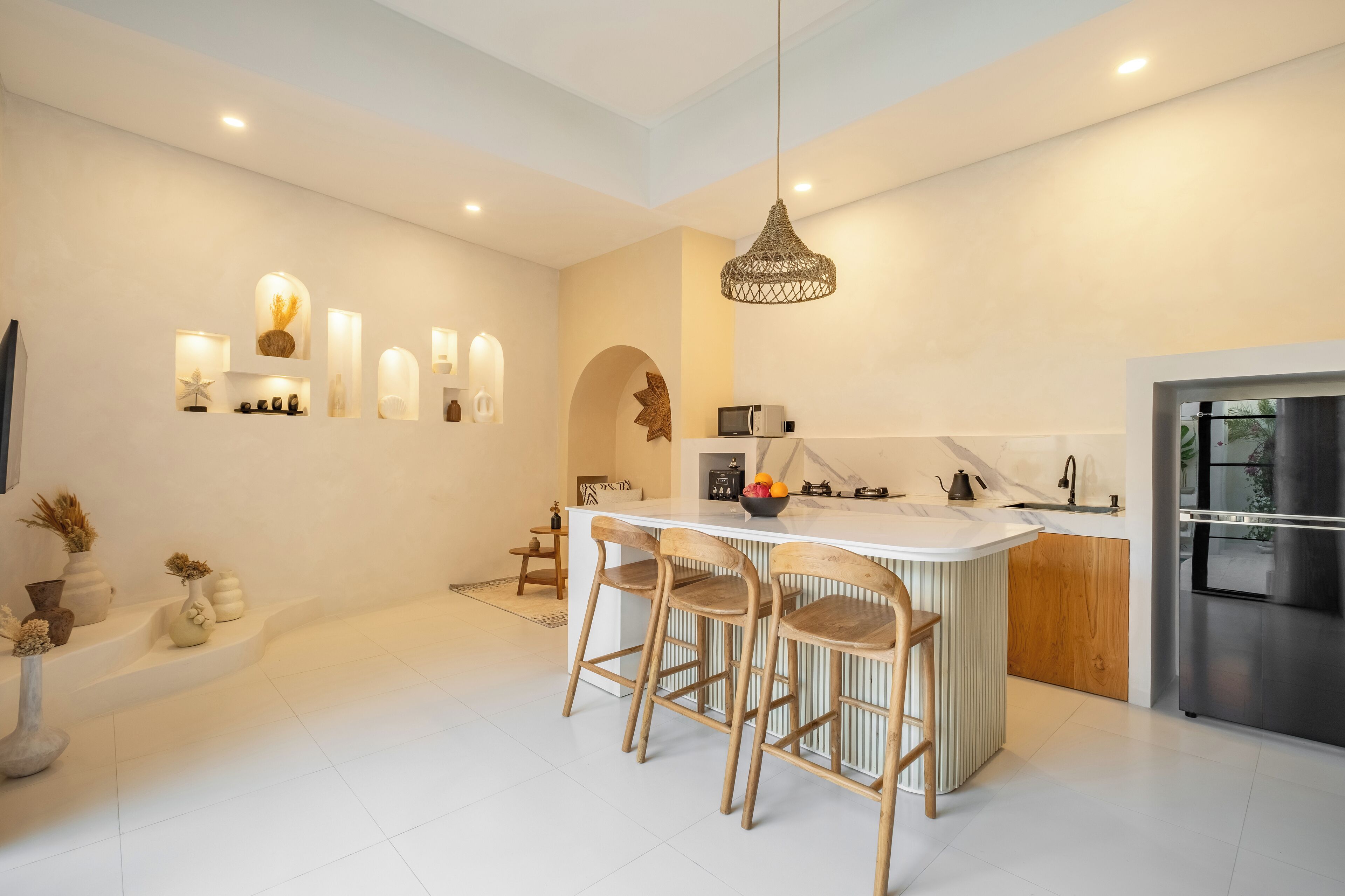 Uma cozinha moderna com uma ilha central, banquetas de bar, uma geladeira e prateleiras decorativas na parede.