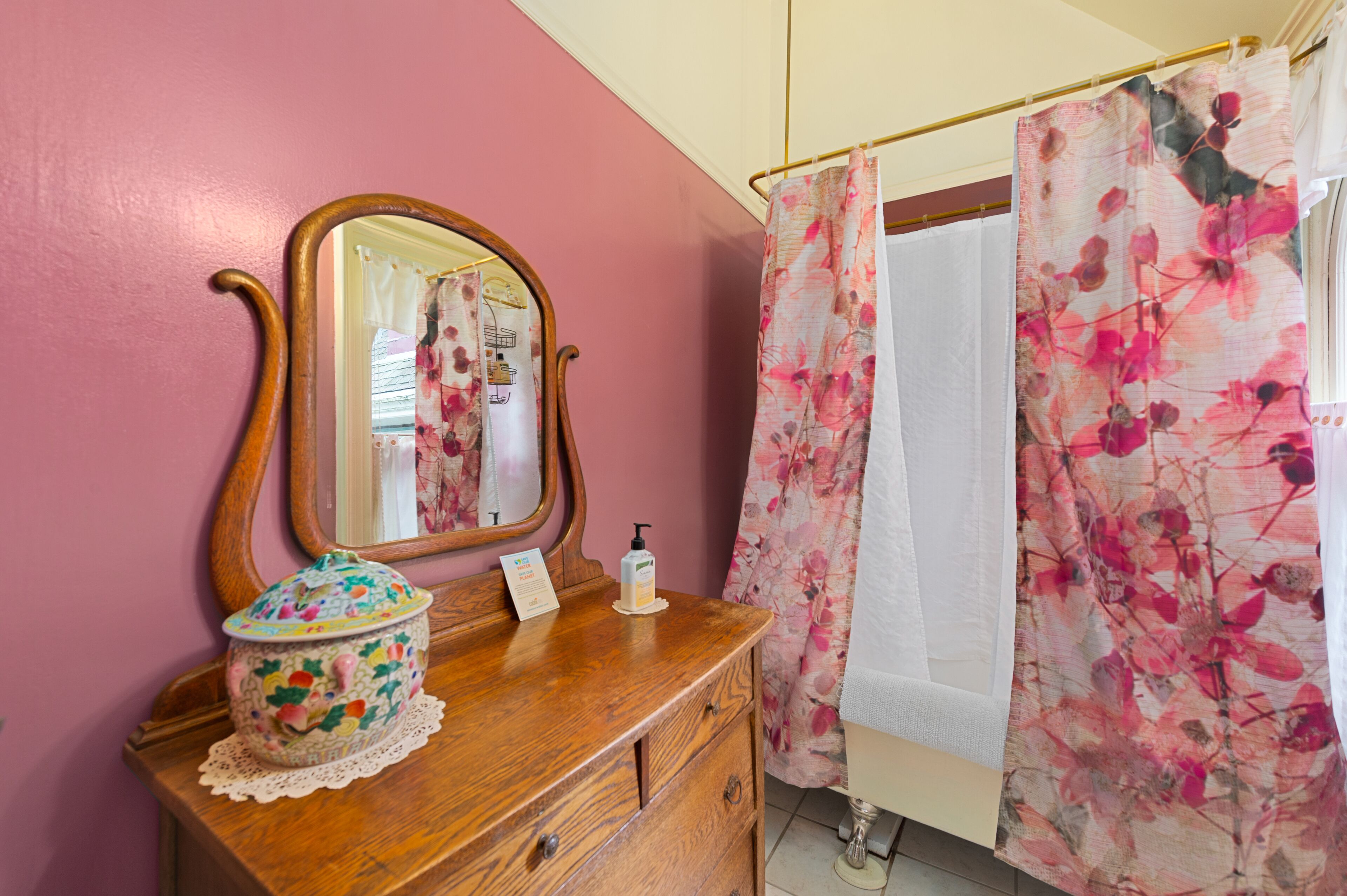 Um banheiro com toucador de madeira, cortina de chuveiro estampada com flores e espelho com moldura decorativa.