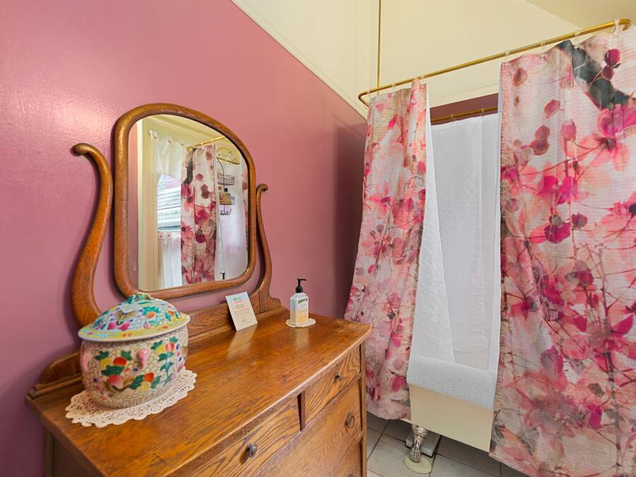 Um banheiro com toucador de madeira, cortina de chuveiro estampada com flores e espelho com moldura decorativa.