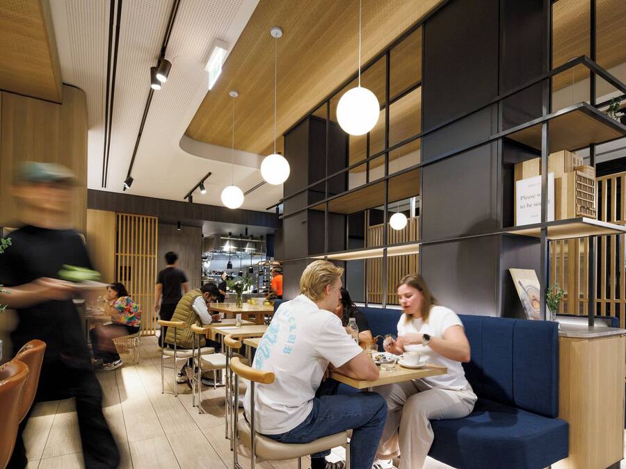 Interior moderno de café, detalhes em madeira, iluminação pendente redonda e cozinha à vista.