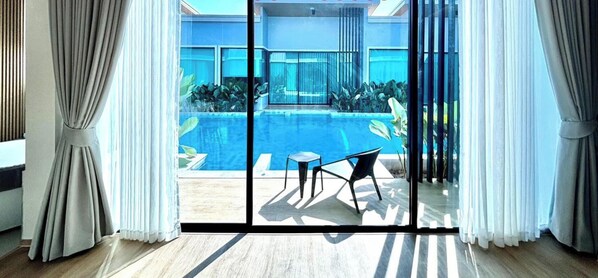 Quarto com vista para uma piscina, grandes janelas e cortinas.