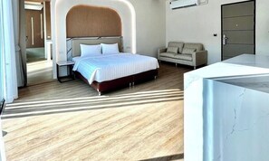Quarto de hotel moderno com uma cama grande, um sofá, uma escrivaninha e um banheiro visível ao fundo.