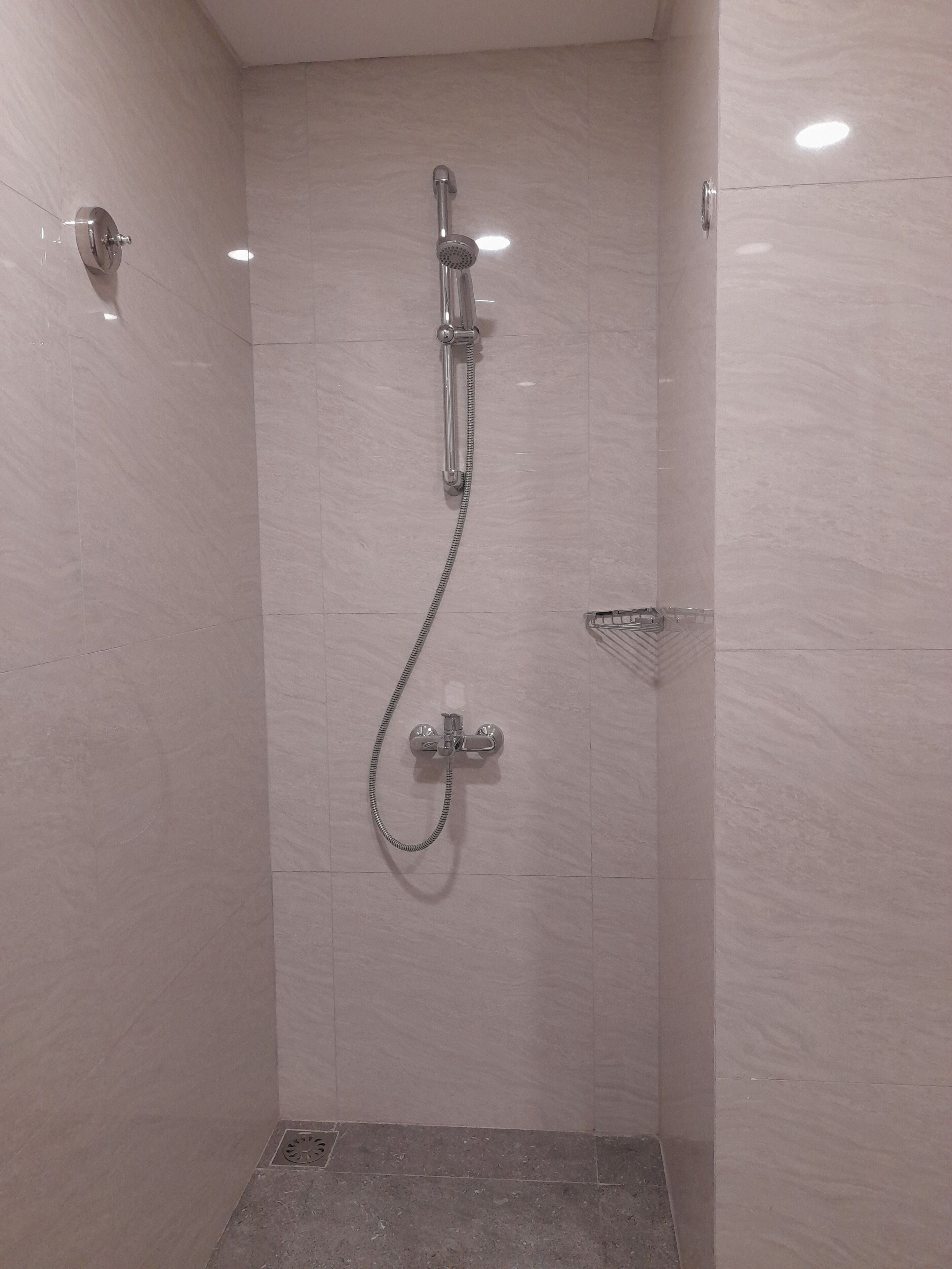 Um chuveiro pequeno e fechado, com um chuveiro manual, um acessório de chuveiro manual e uma torneira fixada na parede.