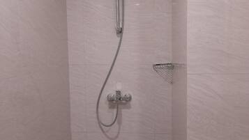 Um chuveiro pequeno e fechado, com um chuveiro manual, um acessório de chuveiro manual e uma torneira fixada na parede.