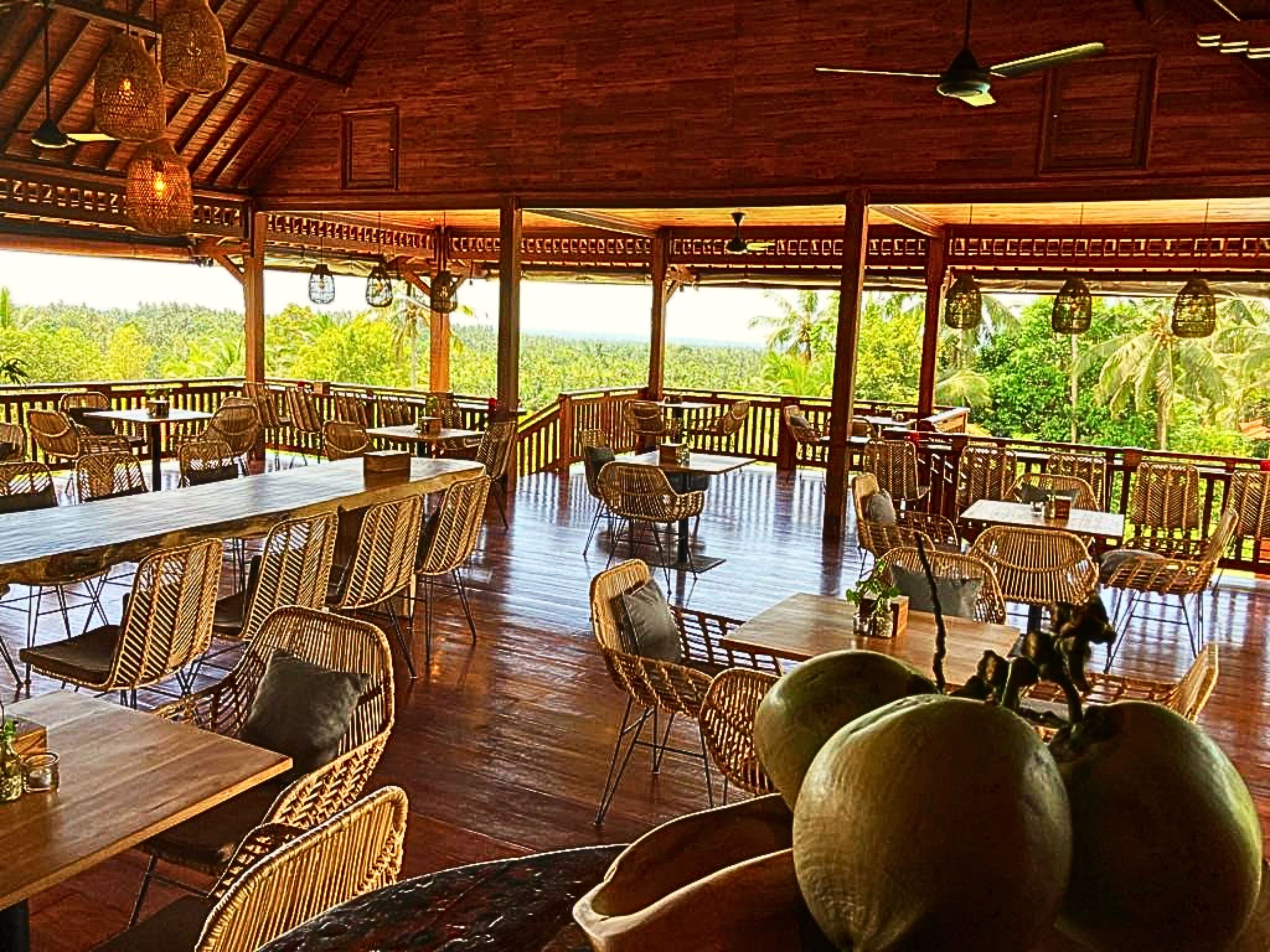 Uma área de refeições ao ar livre com móveis de vime e deck de madeira, com vista para uma paisagem verde exuberante.