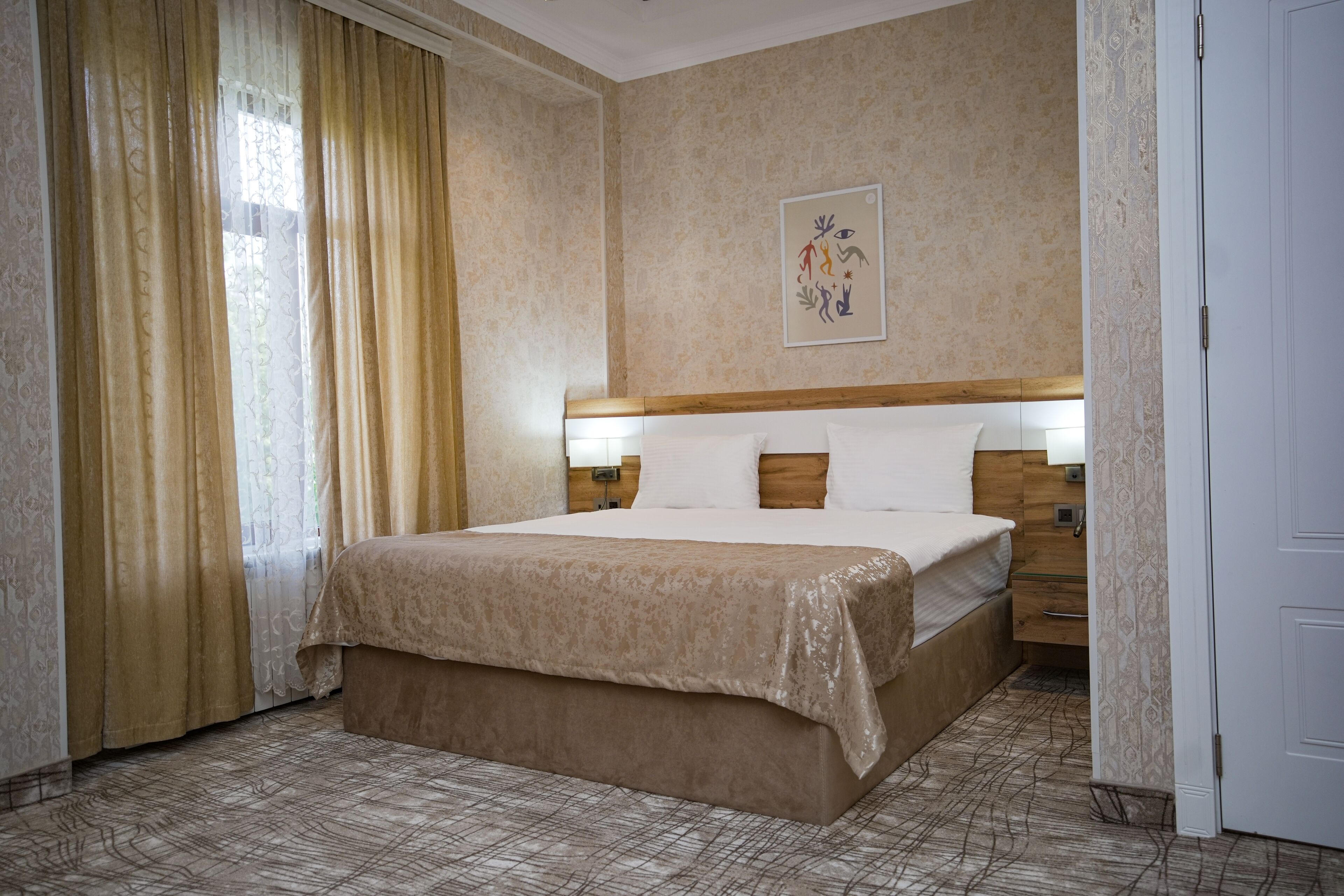 Quarto de hotel com cama grande, mesa de cabeceira, obra de arte na parede e tapete estampado.