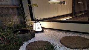 Um jardim japonês tradicional com elementos de pedra, um pequeno espelho d'água e uma placa emoldurada.