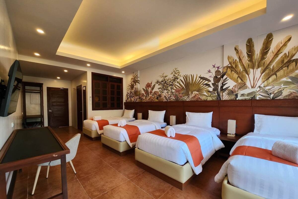 Quarto de hotel com quatro camas, uma escrivaninha e um mural grande na parede.