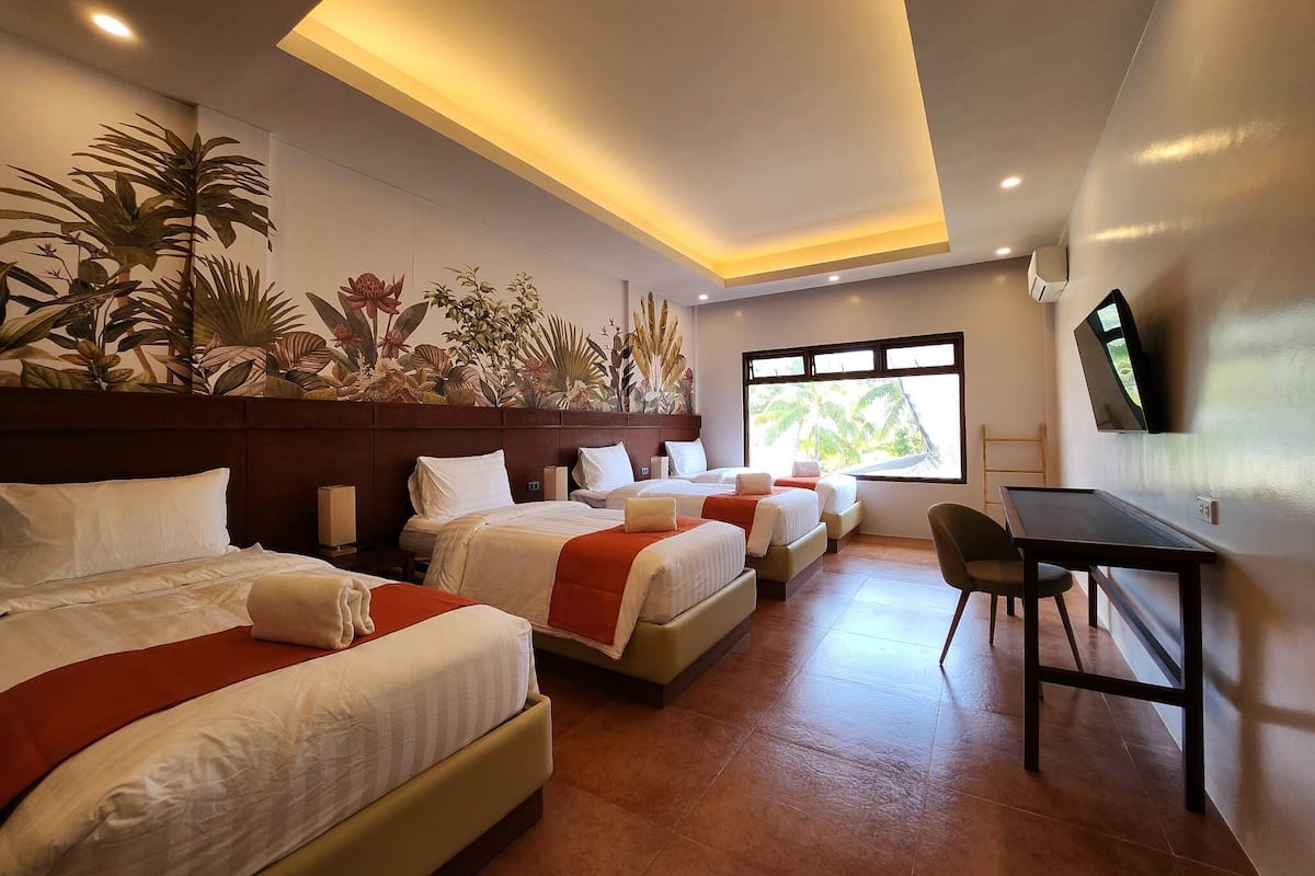Quarto de hotel com três camas, uma mesa e uma televisão.