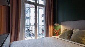 Quarto de hotel com cama, cortinas, vista para o exterior e uma pequena mesa com cadeiras.