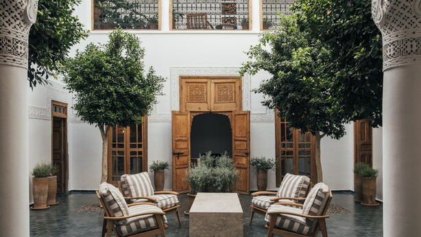 Pátio com duas cadeiras de madeira, uma mesa central e plantas em vasos.