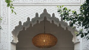 Uma área de estar interna com uma luminária trançada, um vaso de planta e uma vela sobre uma mesa.