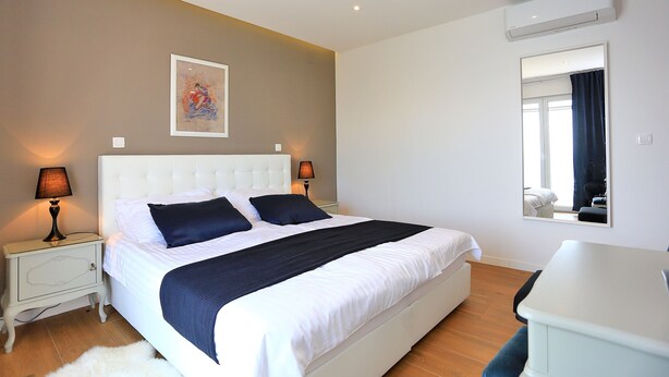 Quarto com cama grande, mesas de cabeceira, escrivaninha e espelho.