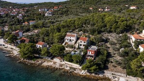 Uma vila costeira com casas numa encosta, vista clara do mar e um litoral rochoso.