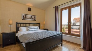 Quarto com cama, mesas de cabeceira, janela com cortinas e um quadro na parede.