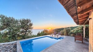 Piscina com vista para o pôr do sol, deck de madeira e espreguiçadeiras.
