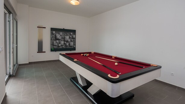 Uma mesa de bilhar com bolas e tacos, um objeto decorativo na parede e uma porta com painel de vidro.