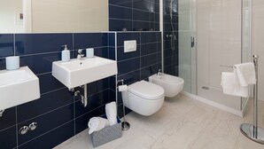 Casa de banho moderna com chuveiro em cabine de vidro, duas pias, sanita e bidé.