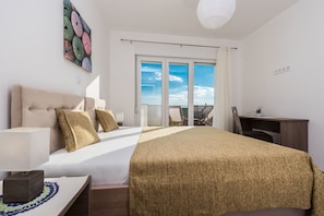 Quarto de hotel moderno com uma cama grande, uma escrivaninha e varanda com vista para o céu.