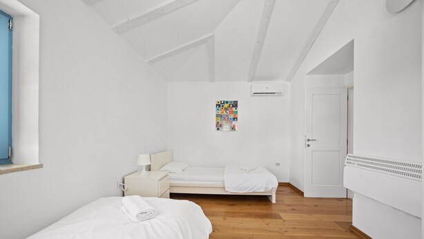 Quarto minimalista com soalho de madeira, uma cama, mesa de cabeceira e ar condicionado fixado na parede.