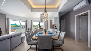 Uma sala de jantar moderna com uma mesa comprida posta para seis pessoas, rodeada por cadeiras estofadas cinzentas.