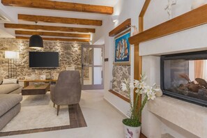 Uma sala de estar com parede de pedra, vigas de madeira, televisão de tela plana, lareira e um sofá.