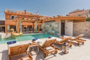 Uma área à beira da piscina com espreguiçadeiras, uma mesa de jantar e um pato inflável grande.