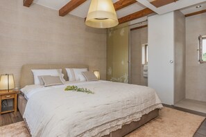 Quarto com cama grande, vigas de madeira no teto, luminária de cabeceira e uma janela.