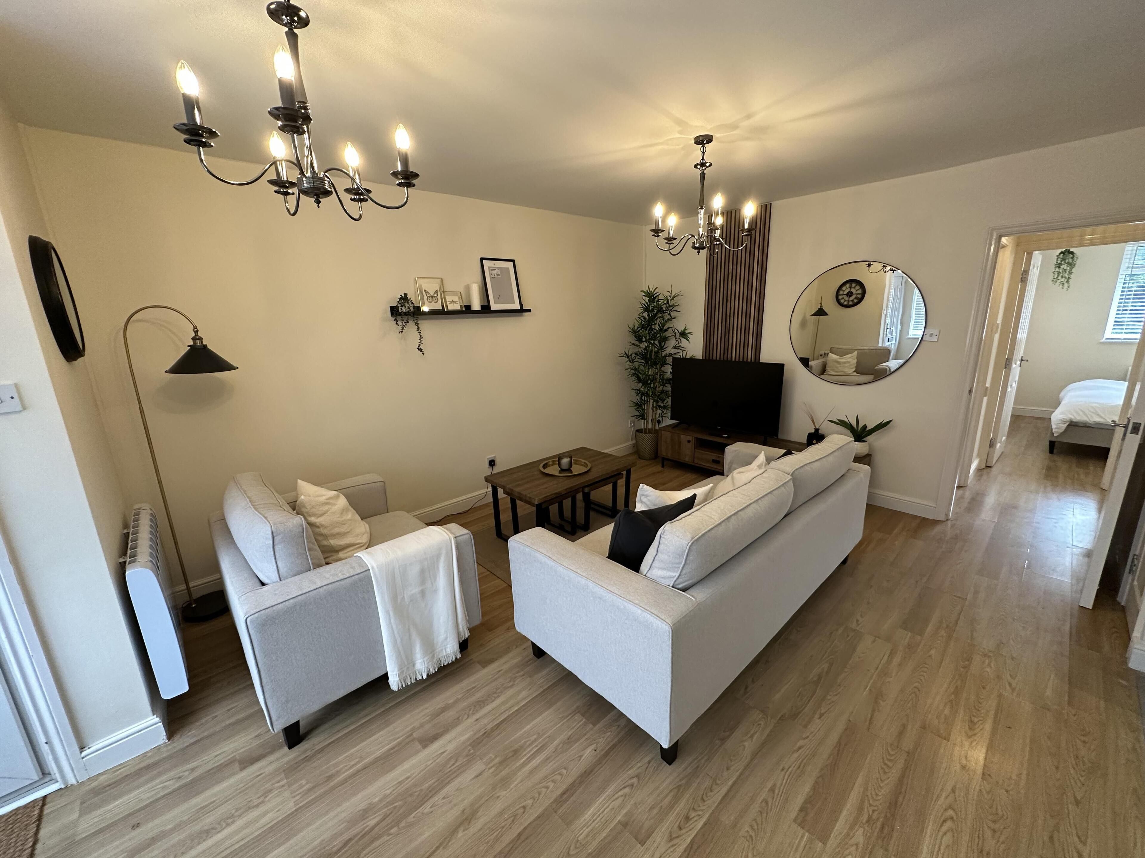 Uma sala de estar com sofá, mesa de centro, televisão, lustre e espelho.
