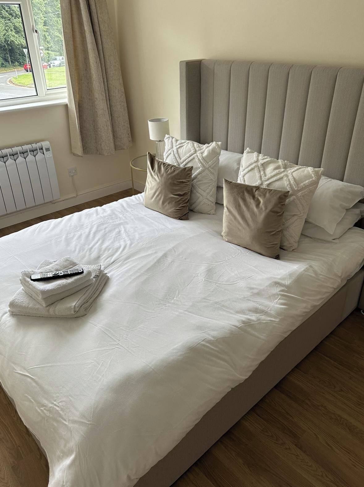 Cama bem arrumada com controle remoto e toalhas dobradas, abajur e vista para o exterior pela janela.