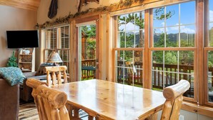 Uma mesa de jantar de madeira com cadeiras, uma televisão e uma lareira num quarto com janelas amplas e vista para o exterior.