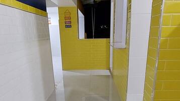 Um corredor com paredes amarelo e branco, piso de azulejos e uma janela no final.