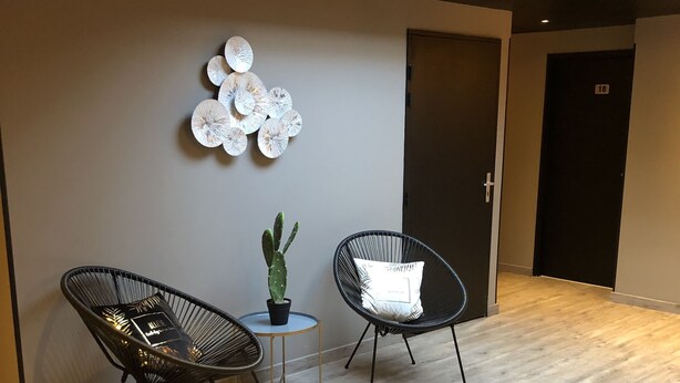 Quarto moderno com duas cadeiras pretas de estrutura vazada, uma mesinha redonda com um cacto em vaso e um objeto decorativo fixado na parede.