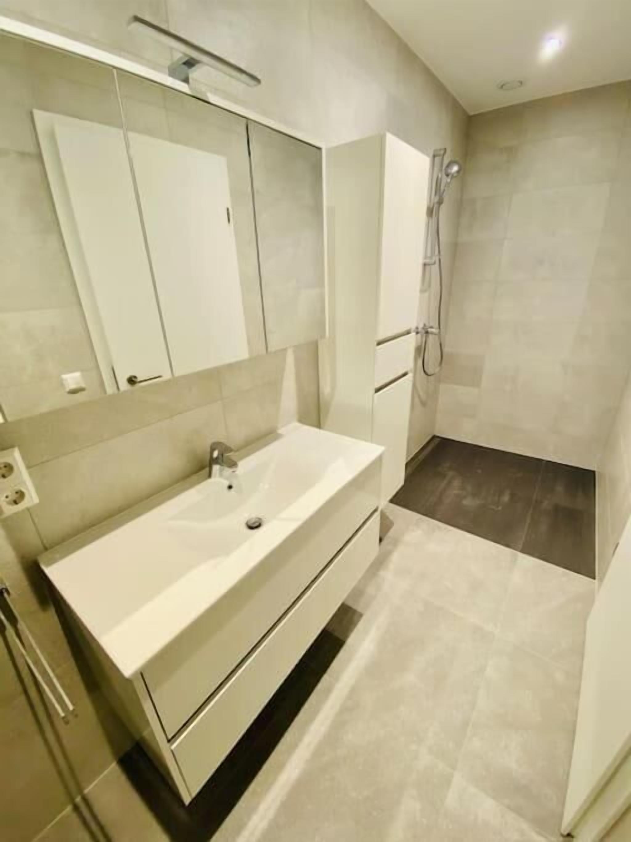 Uma casa de banho moderna com um espelho grande, uma sanita branca e uma área de duche.