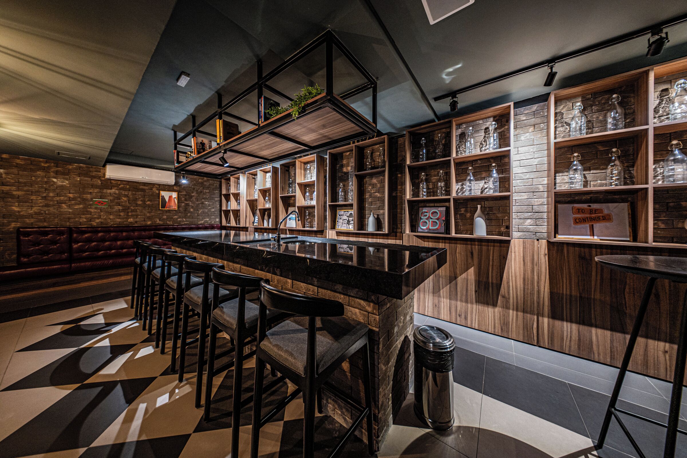 Uma área de bar com balcão alto, banquetes e prateleiras com garrafas.