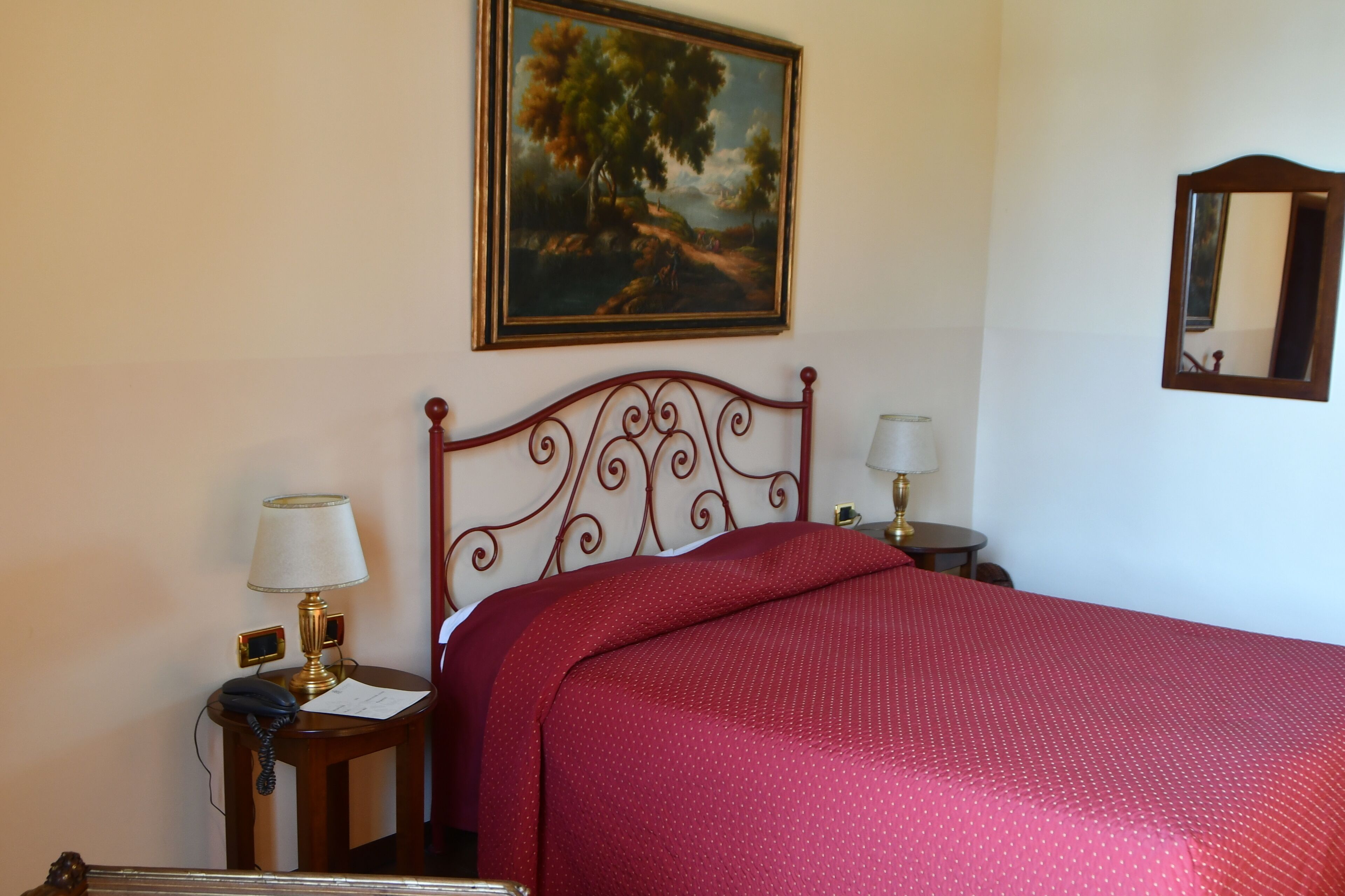 Quarto de hotel com cama, duas mesas de cabeceira, abajur, quadro e espelho.