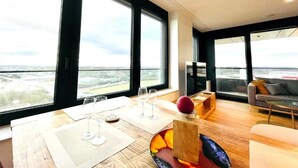 Quarto moderno com grandes janelas, uma mesa de jantar com copos, um sofá e uma televisão.