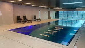 Uma piscina interior moderna com água cristalina, chão em azulejo e espreguiçadeiras ao longo da parede.