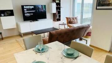 Uma sala de estar moderna com televisão de tela plana, um sofá e um espaço de jantar com pratos e copos verdes.