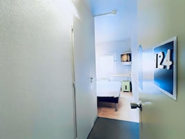 Um corredor com uma cama, uma televisão e uma porta marcada com o número 124.