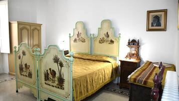 Um quarto com uma cama, um armário de madeira, uma mesinha com uma luminária e um quadro na parede.
