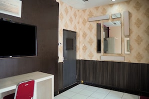 Quarto de hotel com televisão de tela plana na parede, porta com espelho acima e chão ladrilhado.
