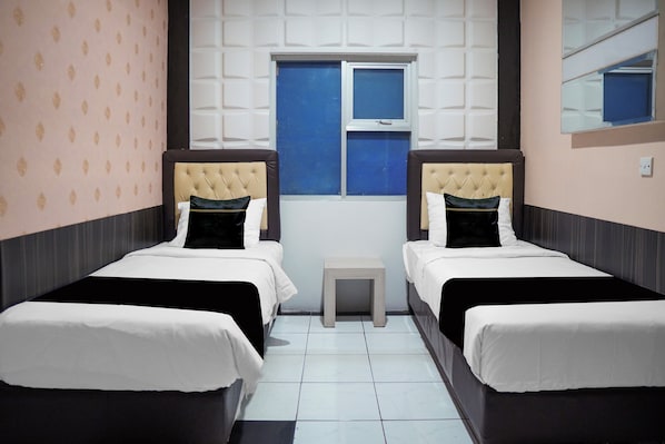 Quarto de hotel com duas camas, uma mesinha e uma janela.