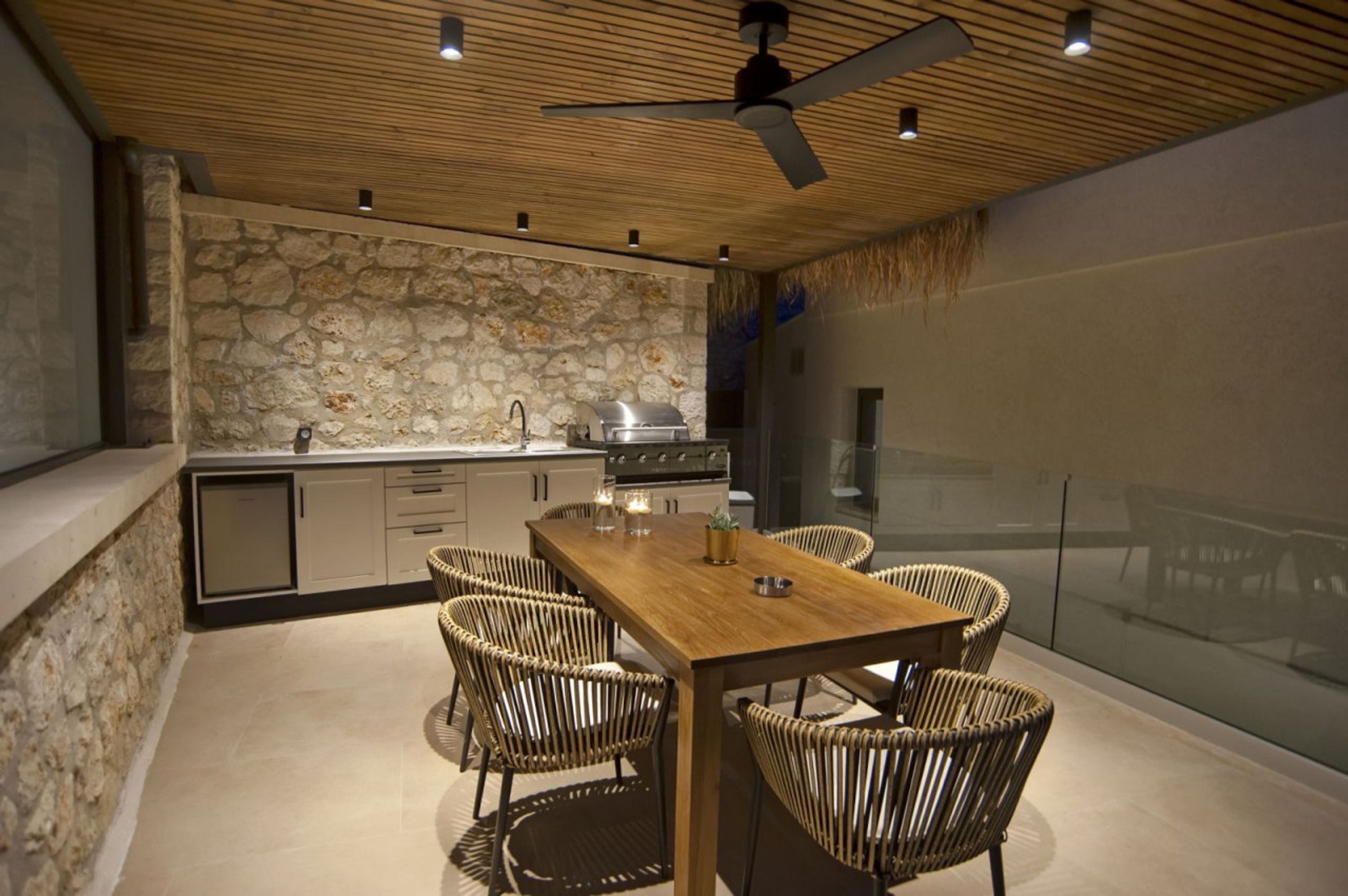 Uma cozinha moderna com paredes de pedra, teto de madeira e um espaço de refeições com cadeiras de vime.