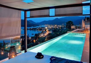 Piscina infinita moderna com vista para uma cidade e montanhas ao entardecer.