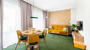 Uma sala de estar moderna com um sofá amarelo, uma mesa de jantar posta com pratos e copos, e um tapete verde.