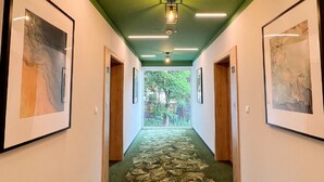 Um corredor com obras de arte emolduradas nas paredes, um tapete verde e vista para árvores através de uma grande janela no final.