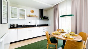 Cozinha moderna com armários brancos, bancada preta e área de refeições com mesa e cadeiras de madeira.