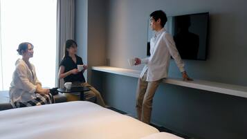 Quarto de hotel com uma cama grande, uma mesa pequena e uma televisão fixada na parede.